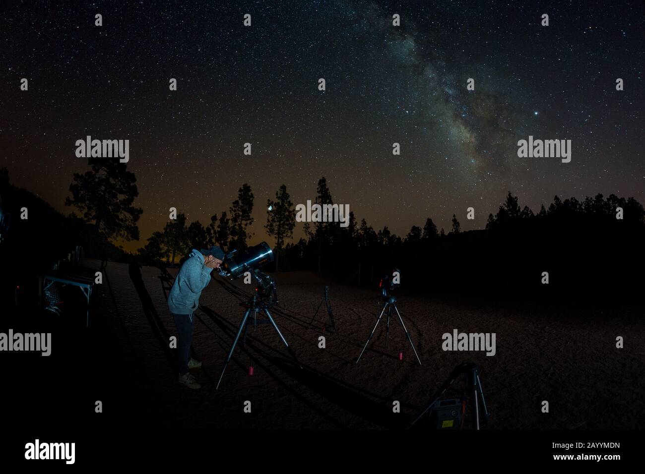 Young man observes starry sky through a telescope. Mountains, surrouded ...
