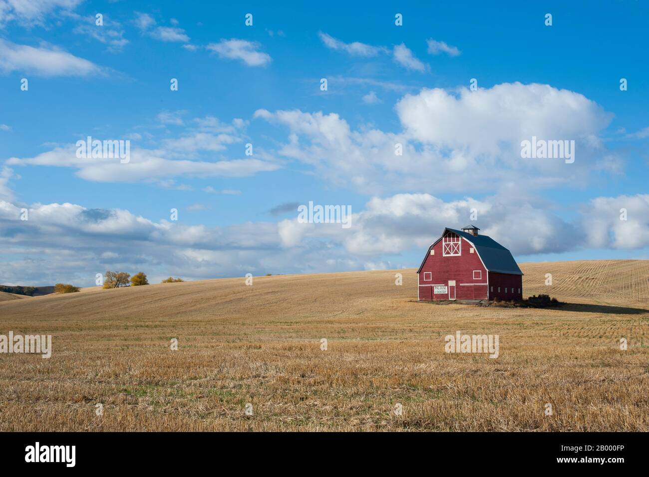 Clouds over a harvested wheat field with a red barn (Palouse Barn) in ...