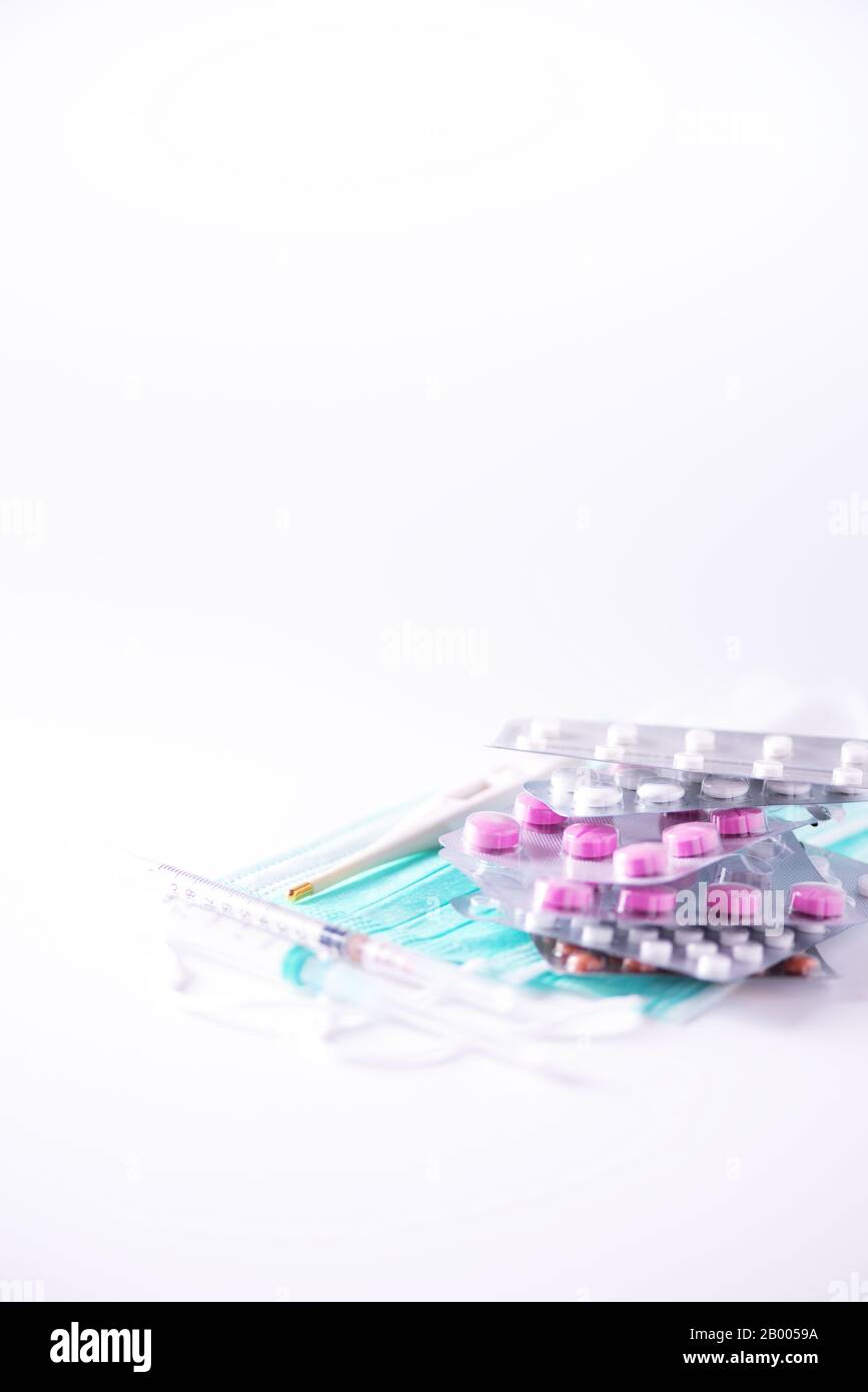 Multicolored pills in blisters, thermometer, protective surgical mask, syringe over white ...