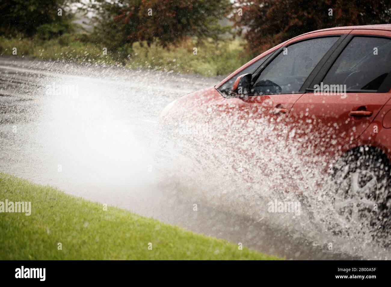 red car on a rainy day driving through a puddle creating a big splash ...