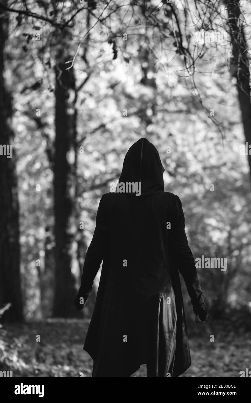 View from the back on a black witch in a mantle during ritual in a ...