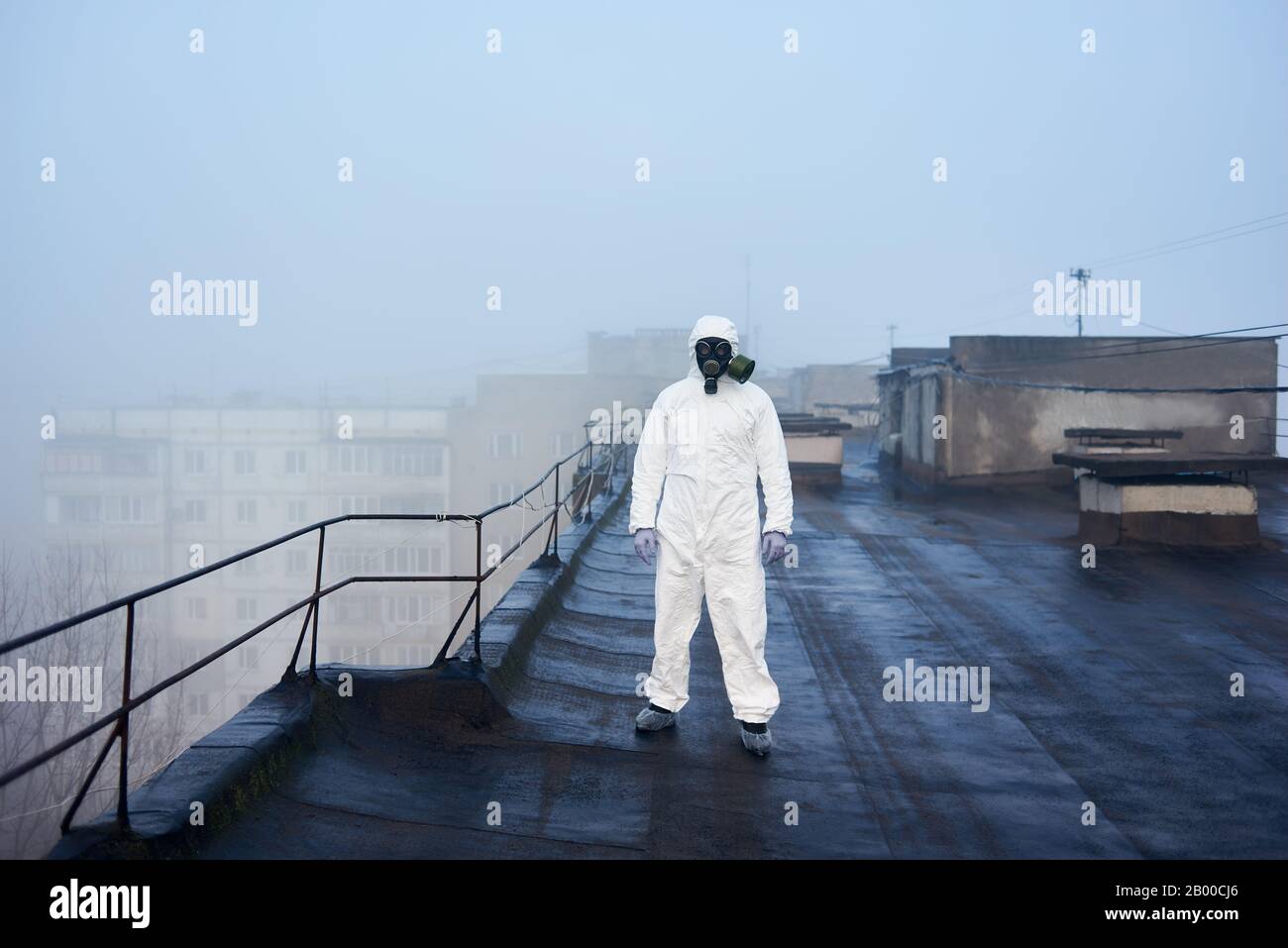 Human standing on the roof of block of flats, wearing white protection ...