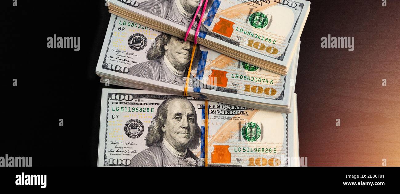 Three packs of one hundred dollar cash bills on a dark table. Lighting ...