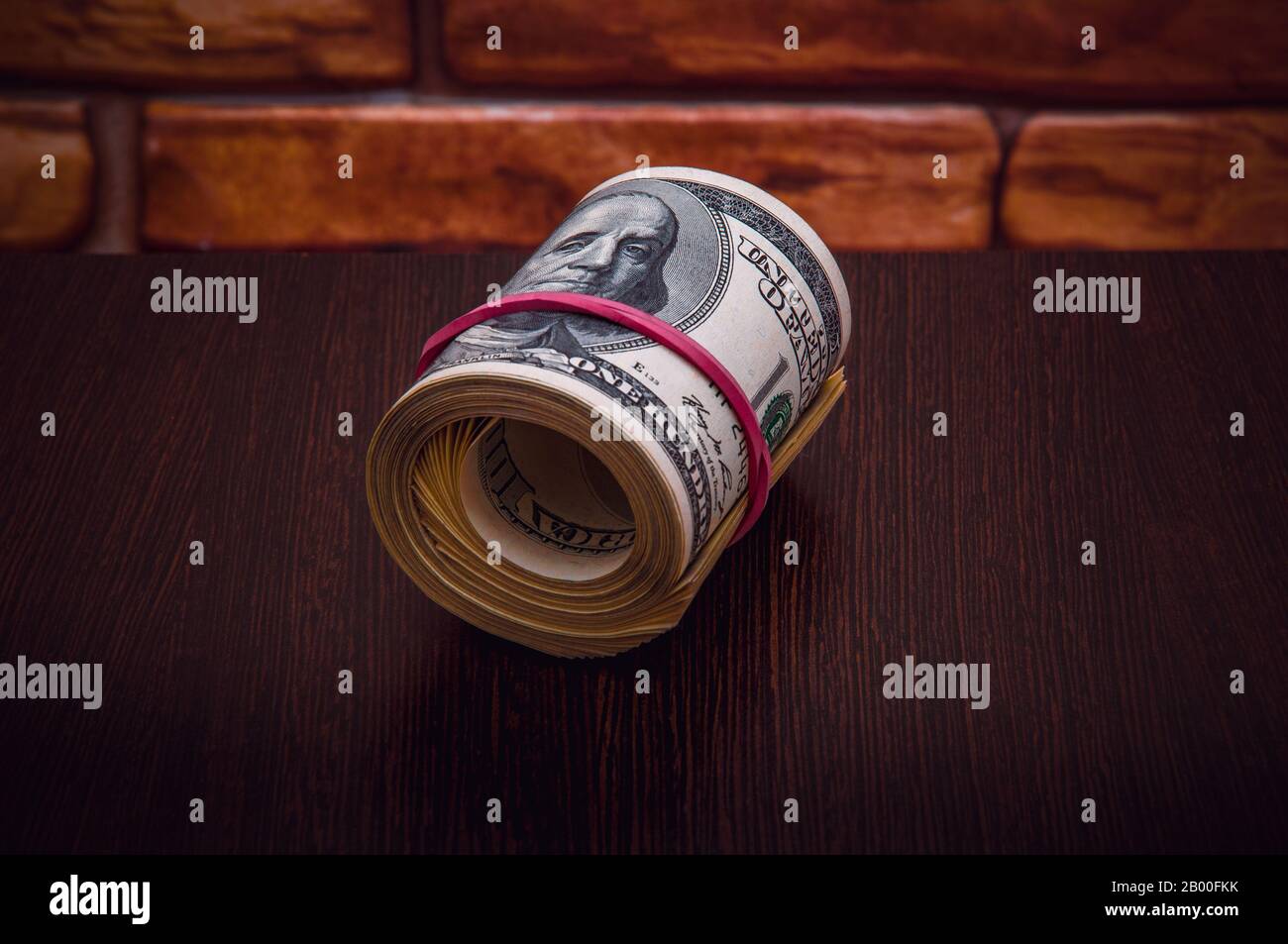 A roll of hundred dollar bills against a brick wall. Close up Stock ...