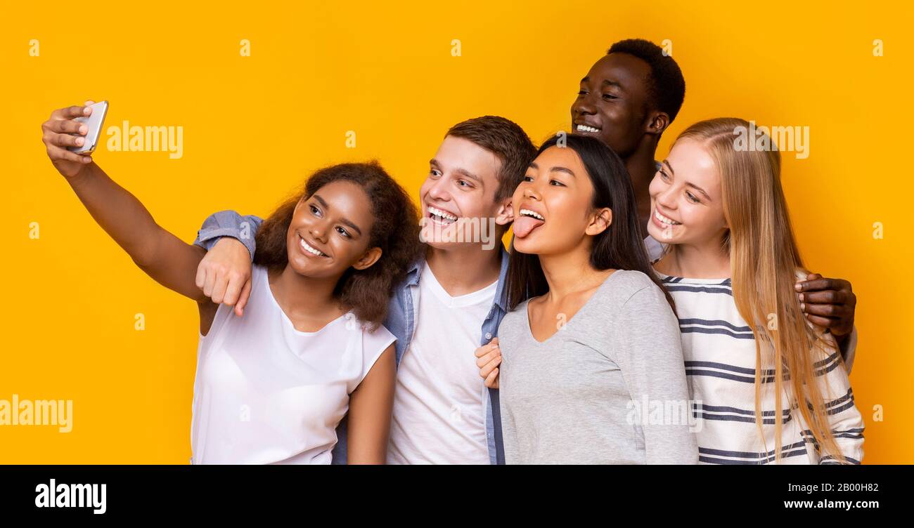 Portrait of smiling friends taking group selfie over yellow background ...