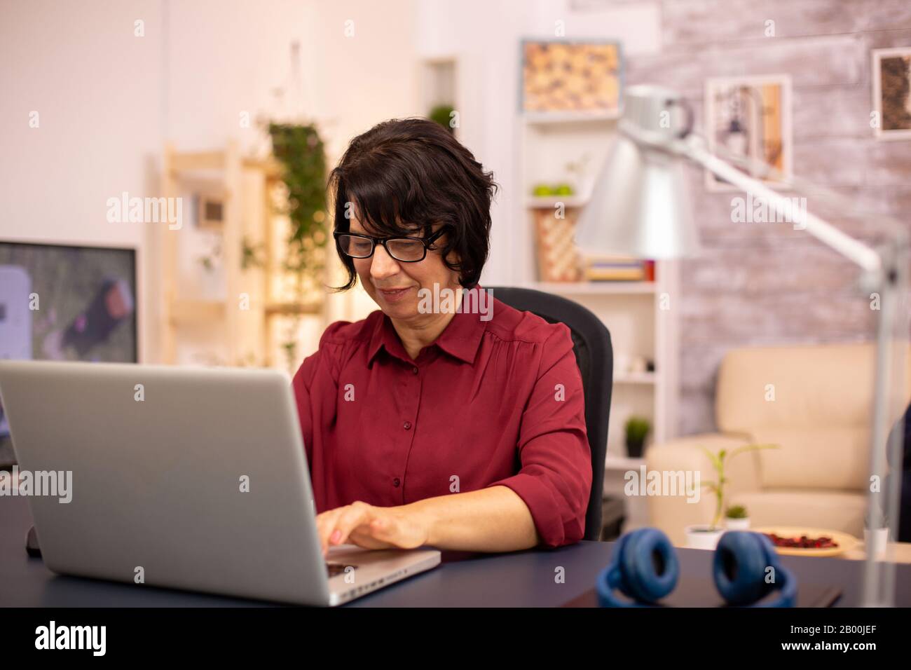 Old woman using a modern computer in her living room while her husband ...