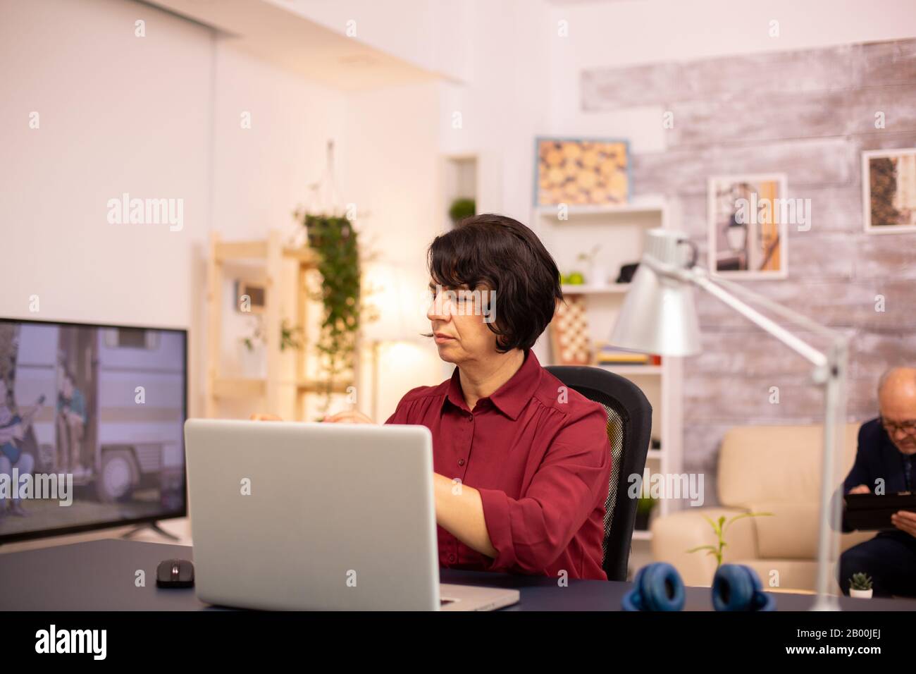 Old woman using a modern computer in her living room while her husband ...