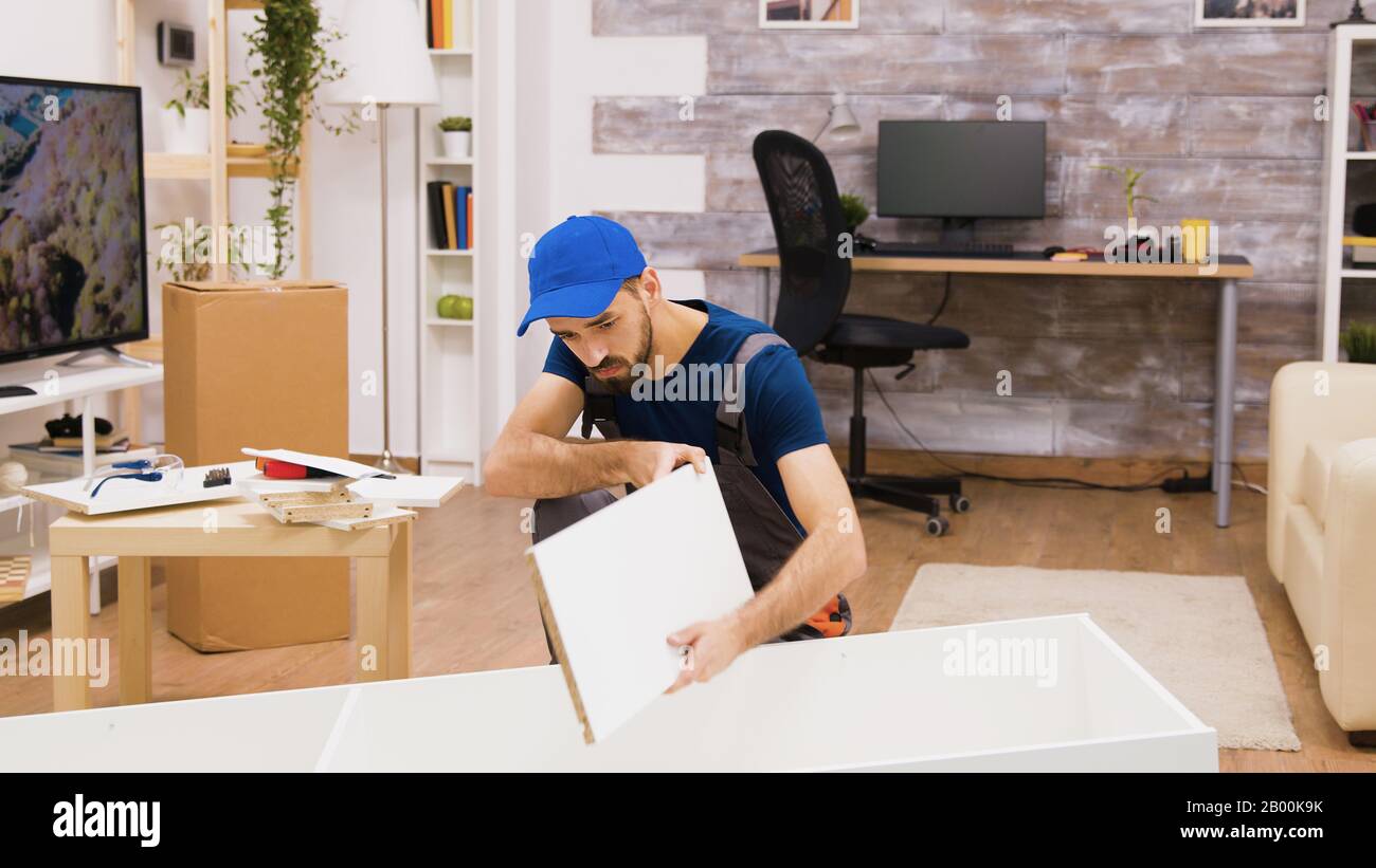 Professional furniture assembly worker wearing a cap while mounting a ...