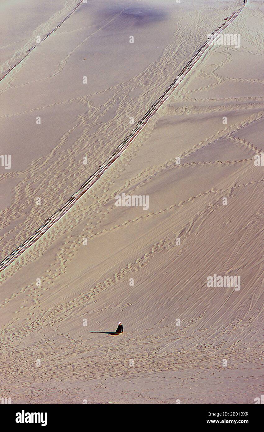 China: A visitor takes a sand sledge down the singing sand dunes of ...