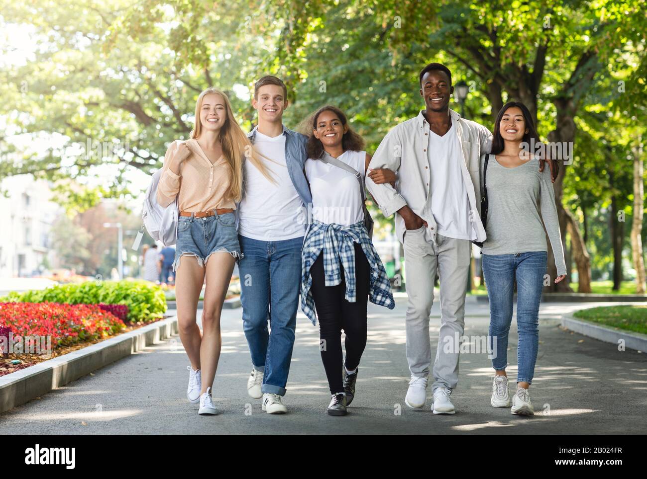 Carefree international students walking together in public park after ...