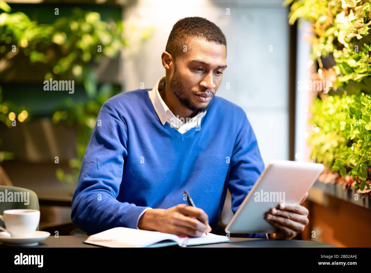 Black business guy taking notes in notebook holding tablet Stock Photo ...