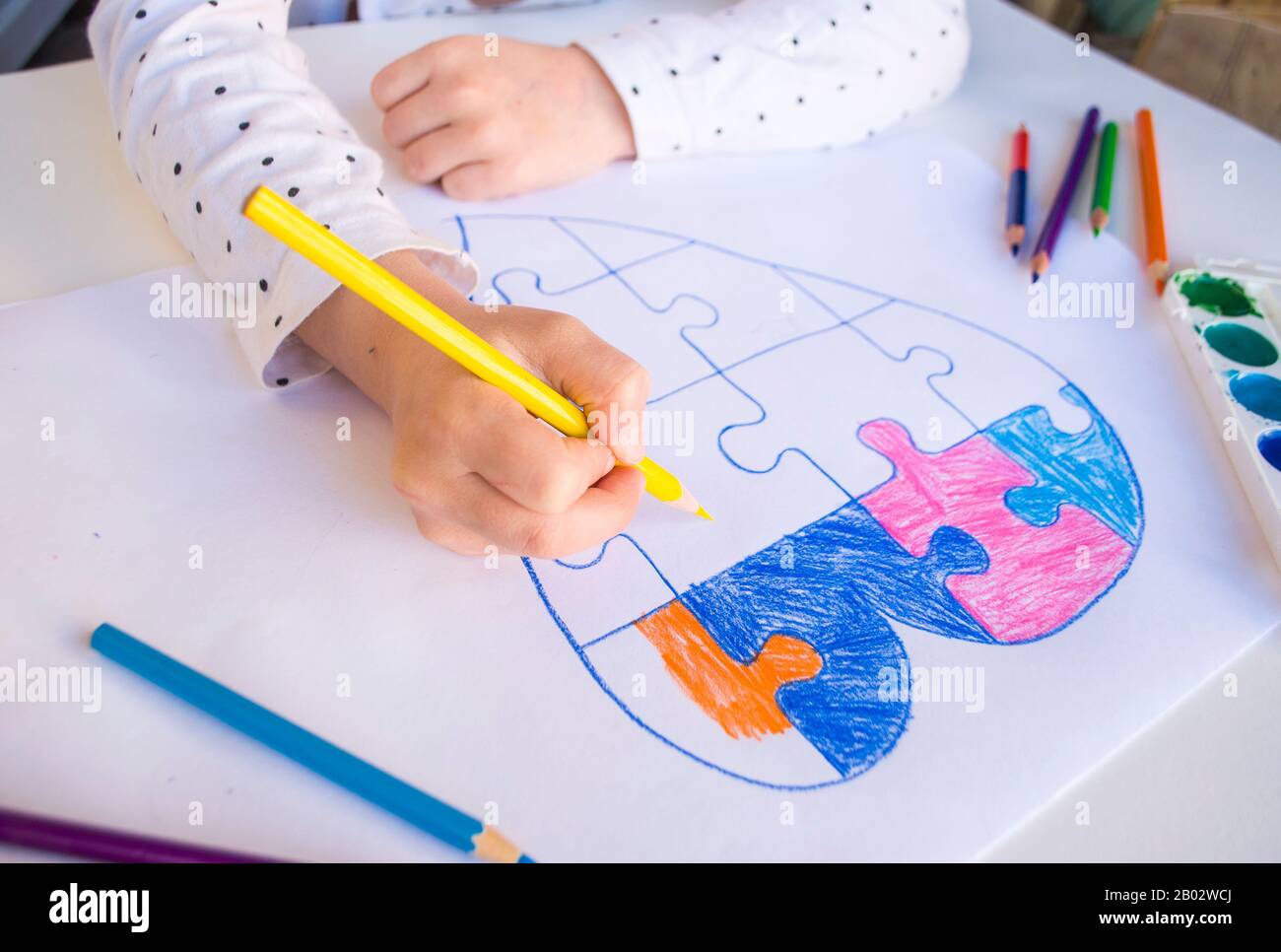 A child is drawing colorful heart with jigsaw puzzle on white ...