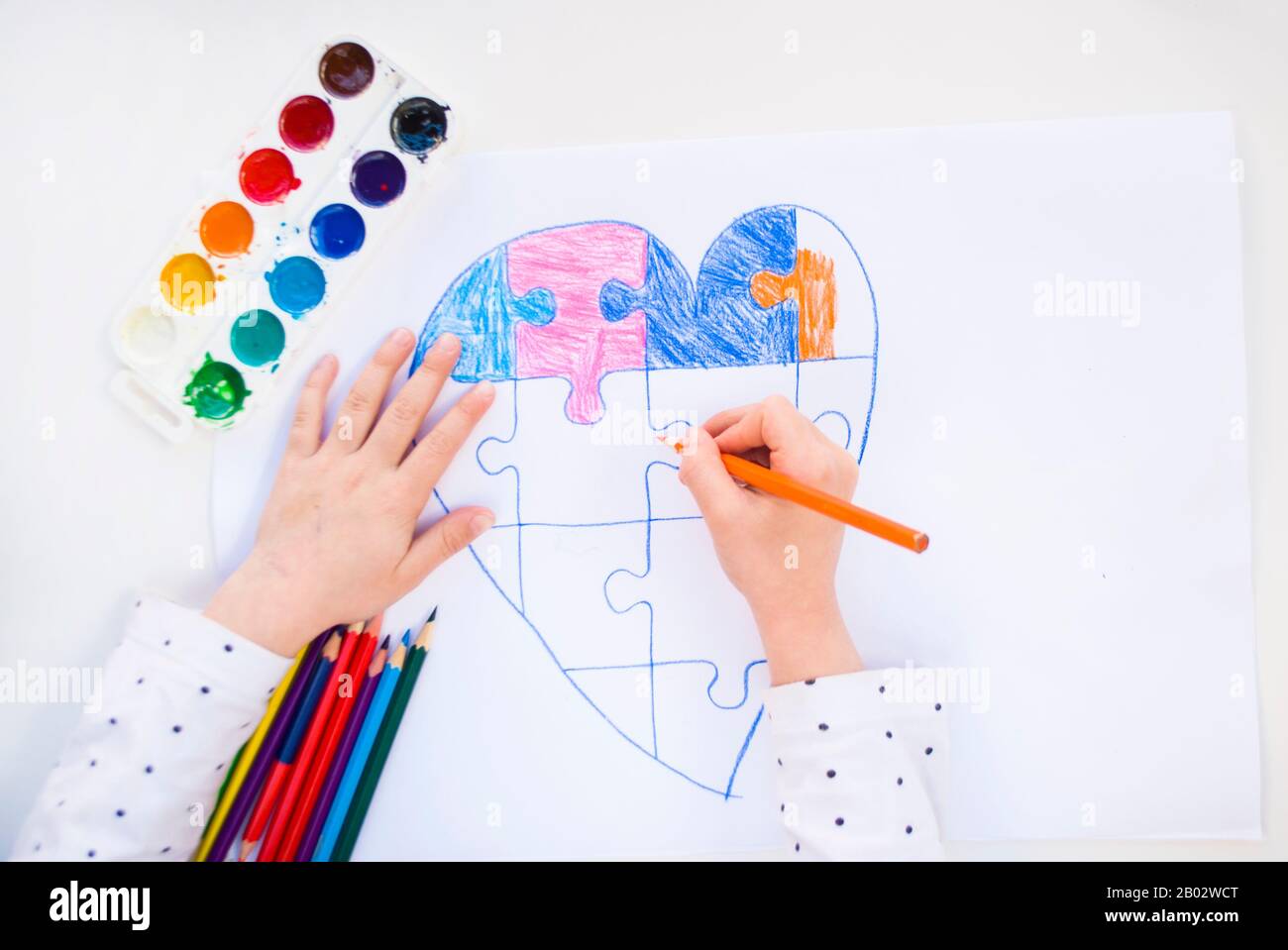 A child is drawing colorful heart with jigsaw puzzle on white ...