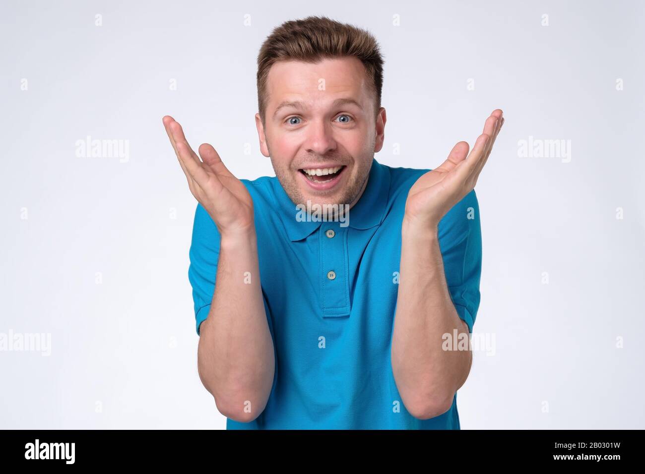 Excited casual man standing with raised hands and looking at camera ...