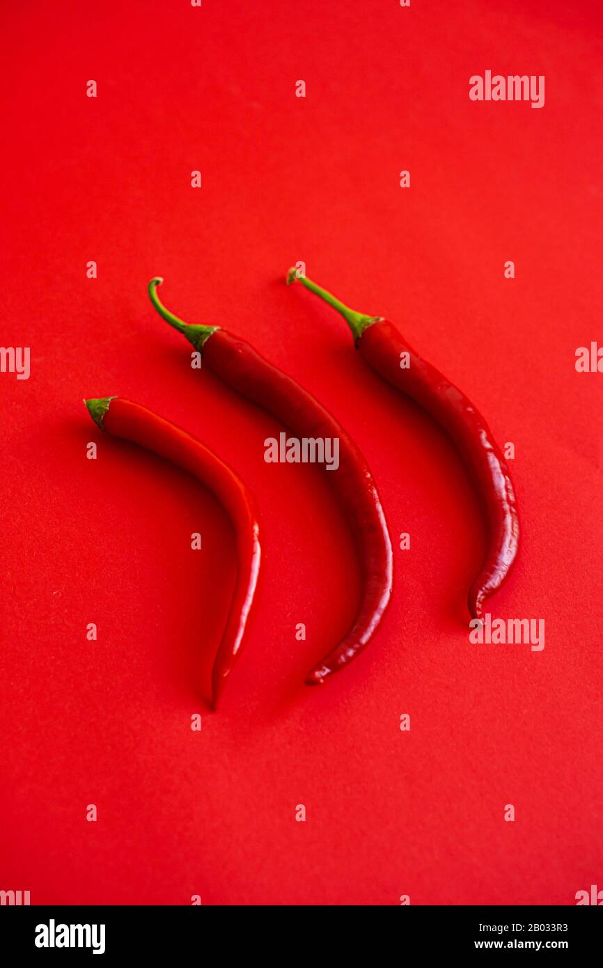 Three red chili peppers on flat red background Stock Photo - Alamy