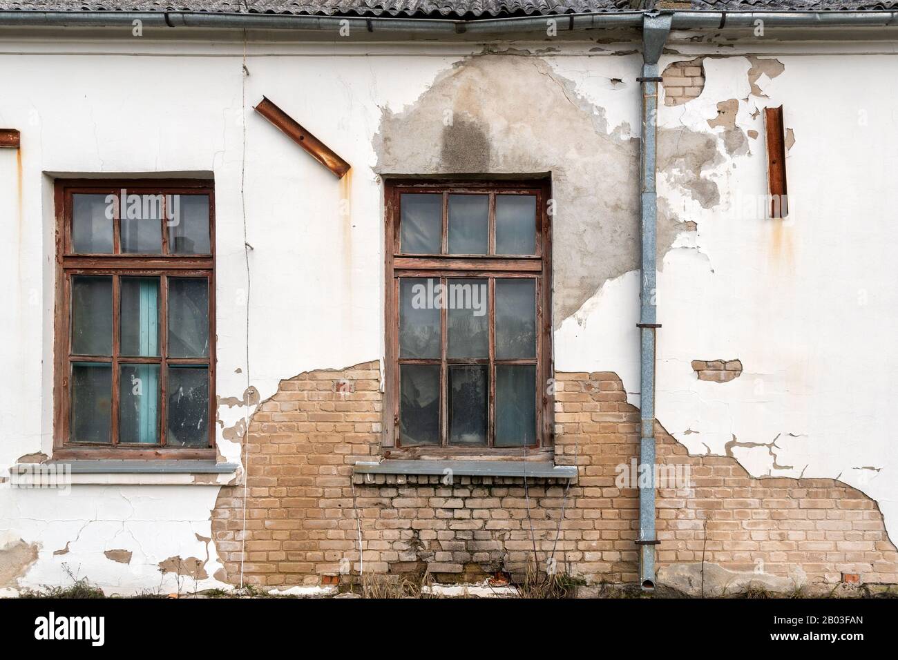 Two windows in damaged wall of an abandoned house. An outside window ...