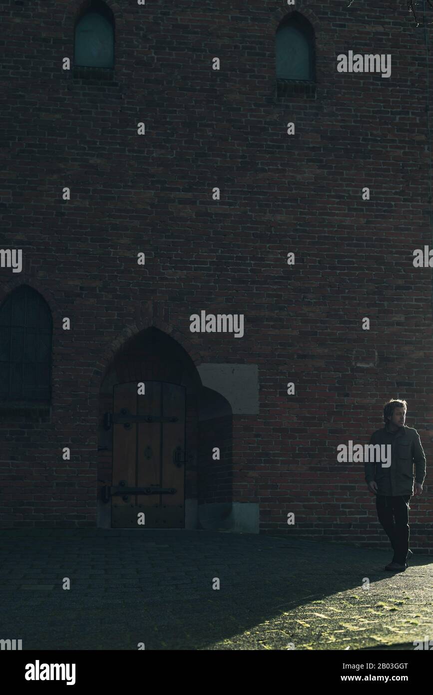 Man in green jacket walking on pavement near church Stock Photo - Alamy
