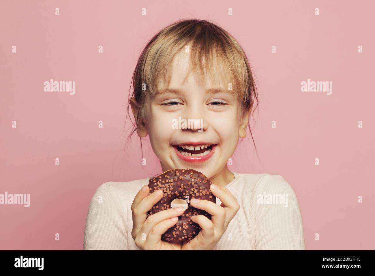 Cute little girl laughing and having fun with chocolate donut on pink ...