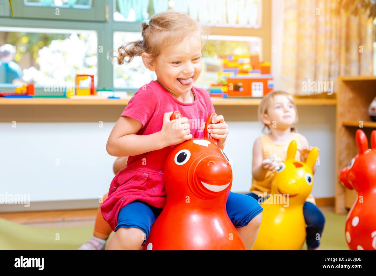 Little girls riding on play horses in kindergarten Stock Photo - Alamy