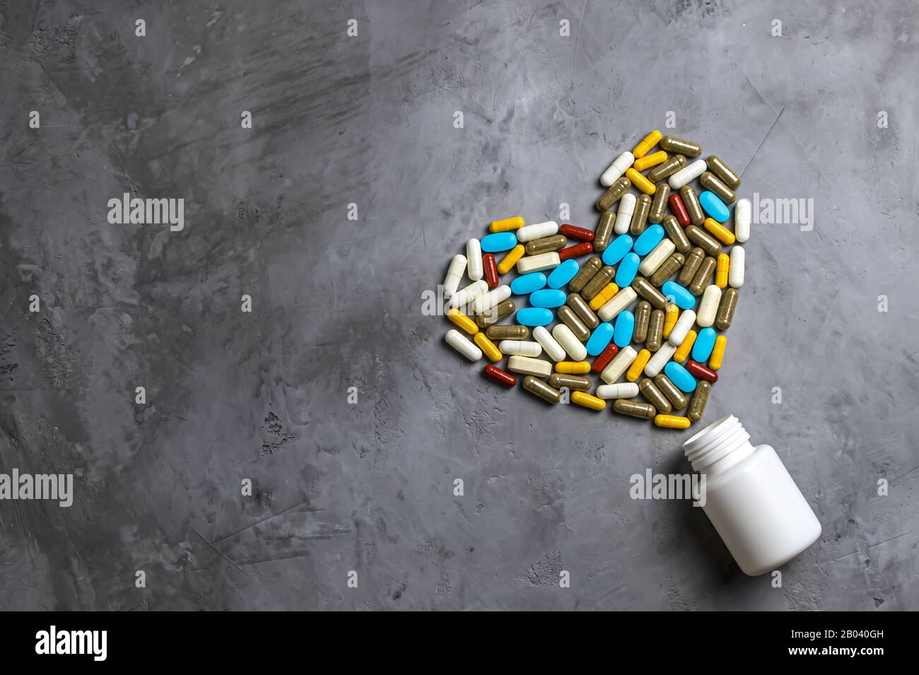 White bottle and multi-colored pills in shape of a heart. Gray concrete ...