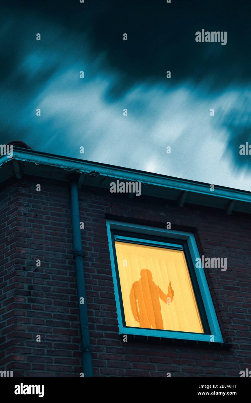Burglar with pistol in eerie house with illuminated window under stormy ...