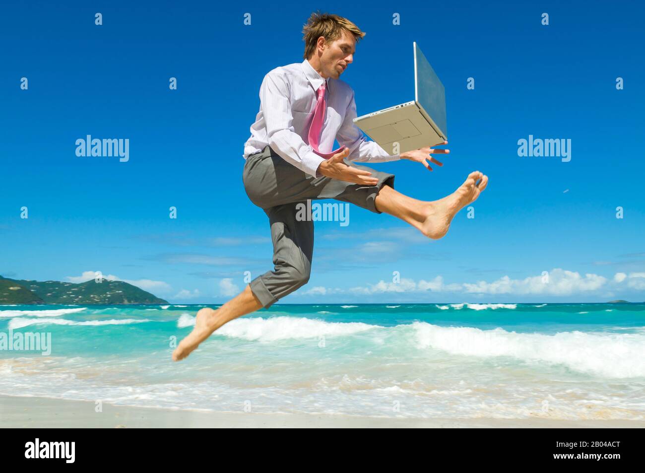 Energetic office worker jumping with his laptop along the shore of an ...