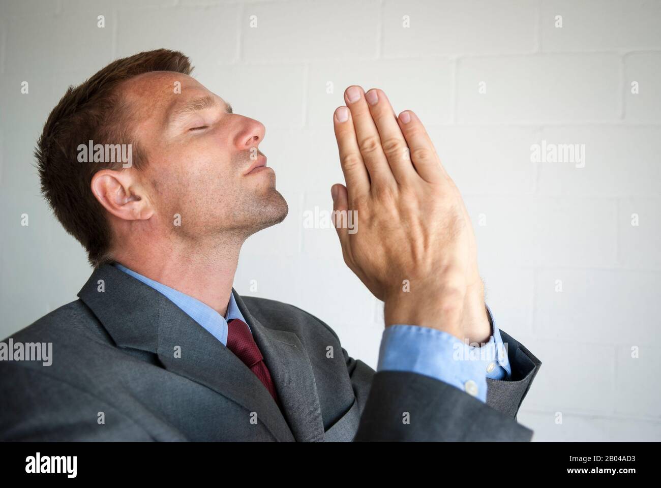 Religious businessman folding his hands in prayer facing his head ...