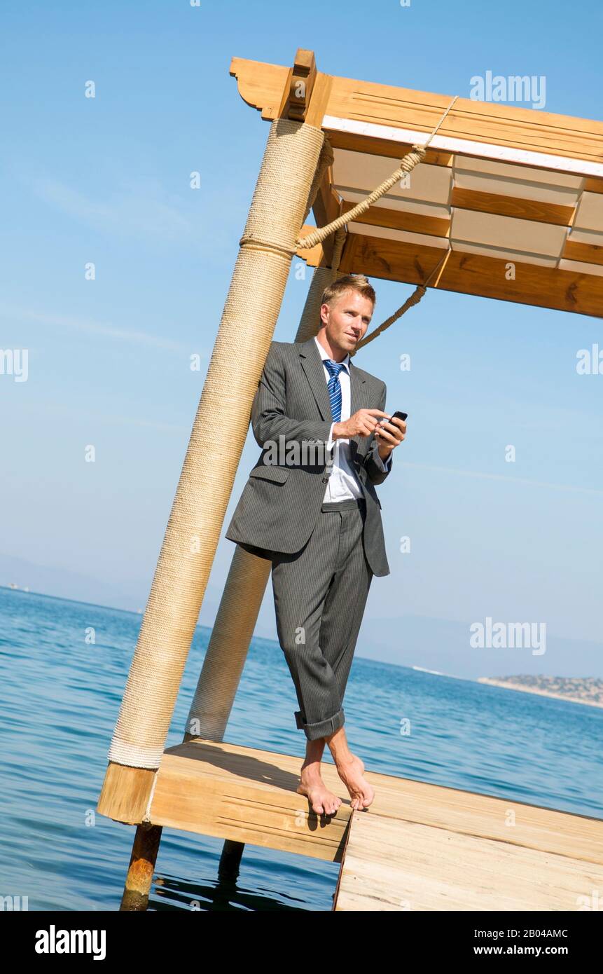 Barefoot businessman relaxing with his smartphone standing outdoors on ...
