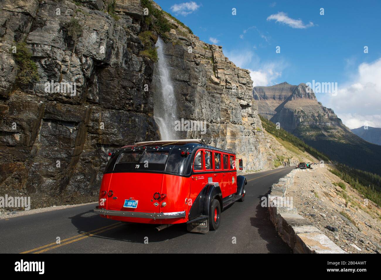 Red tour bus at waterfall coming down next to the Going-to-the-Sun Road ...