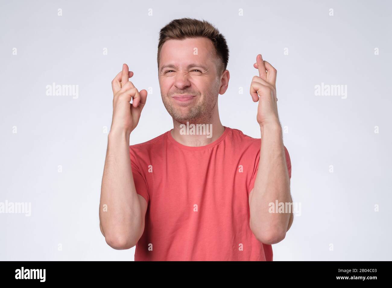 Young man making a wish crossing fingers isolated on white background ...