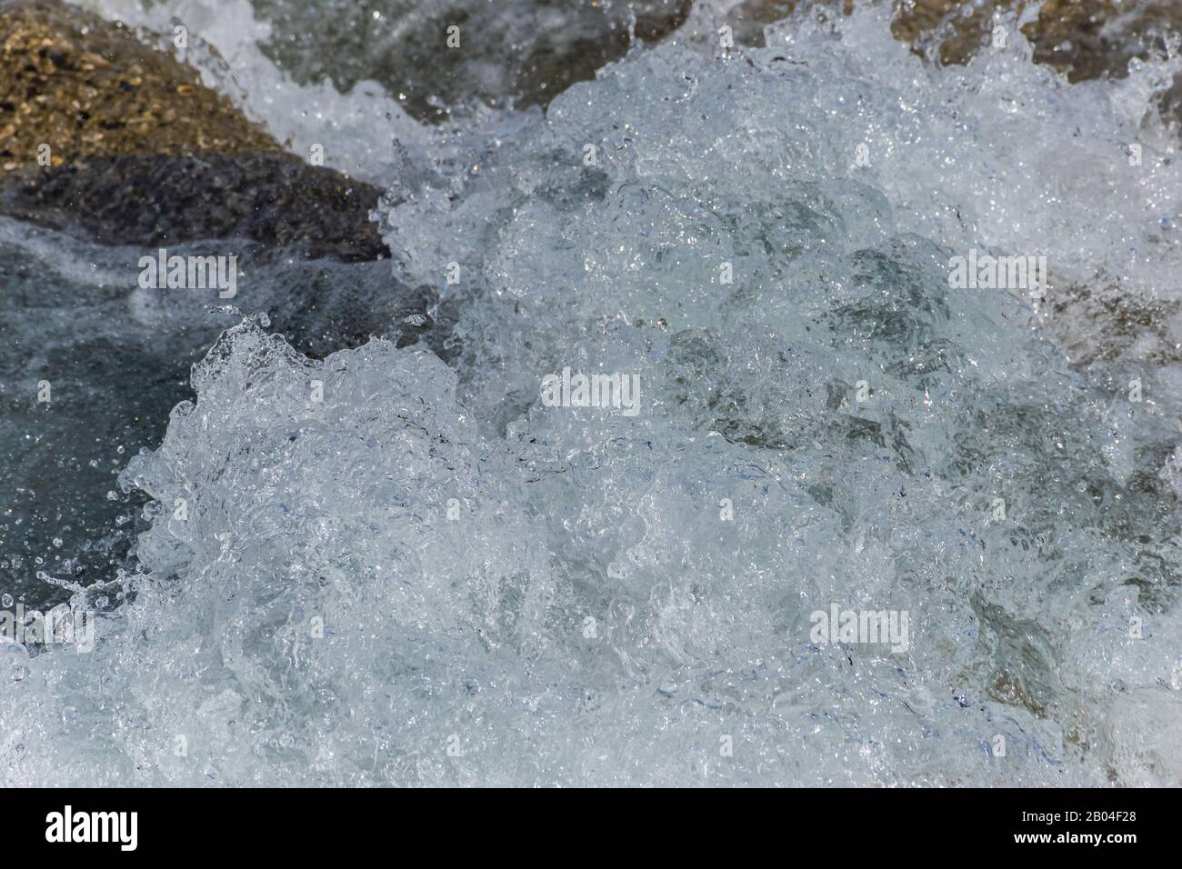 A close-up of a wave splashing over the mountain river cascade boulders ...