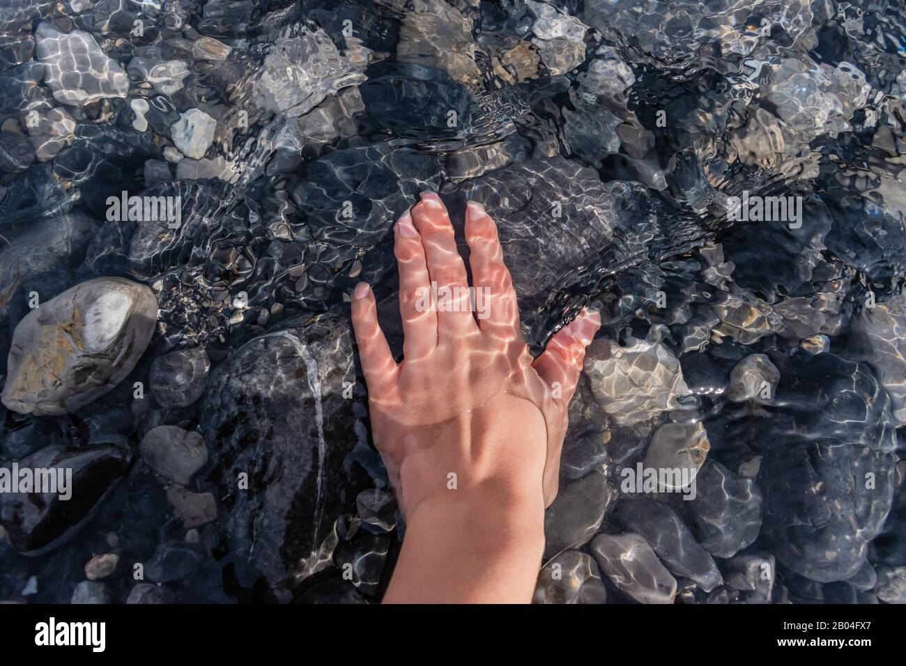 A young woman's hand underwater touching pebbles under clean ...