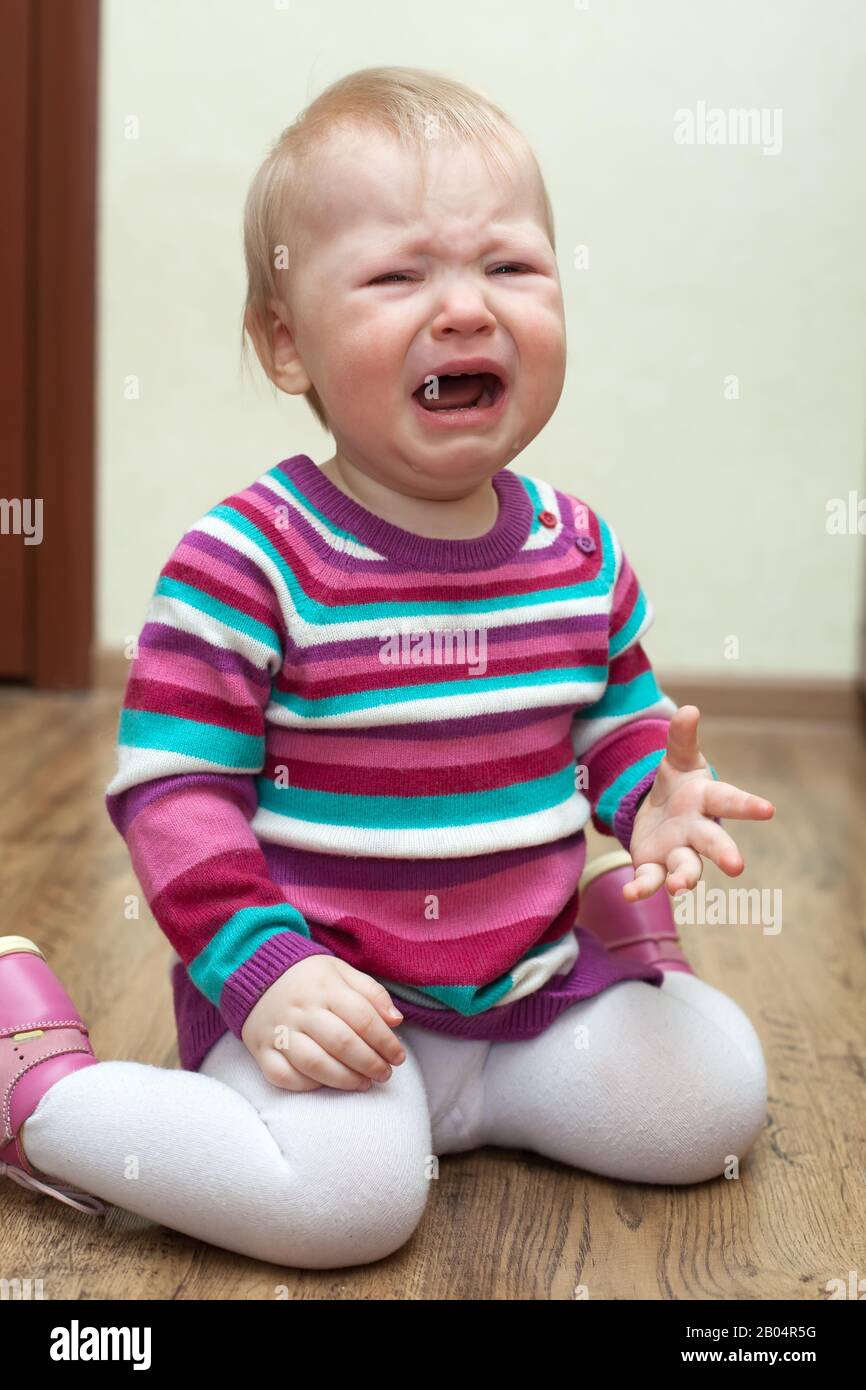 Portrait of crying baby girl sitting on the floor in pink dress Stock ...