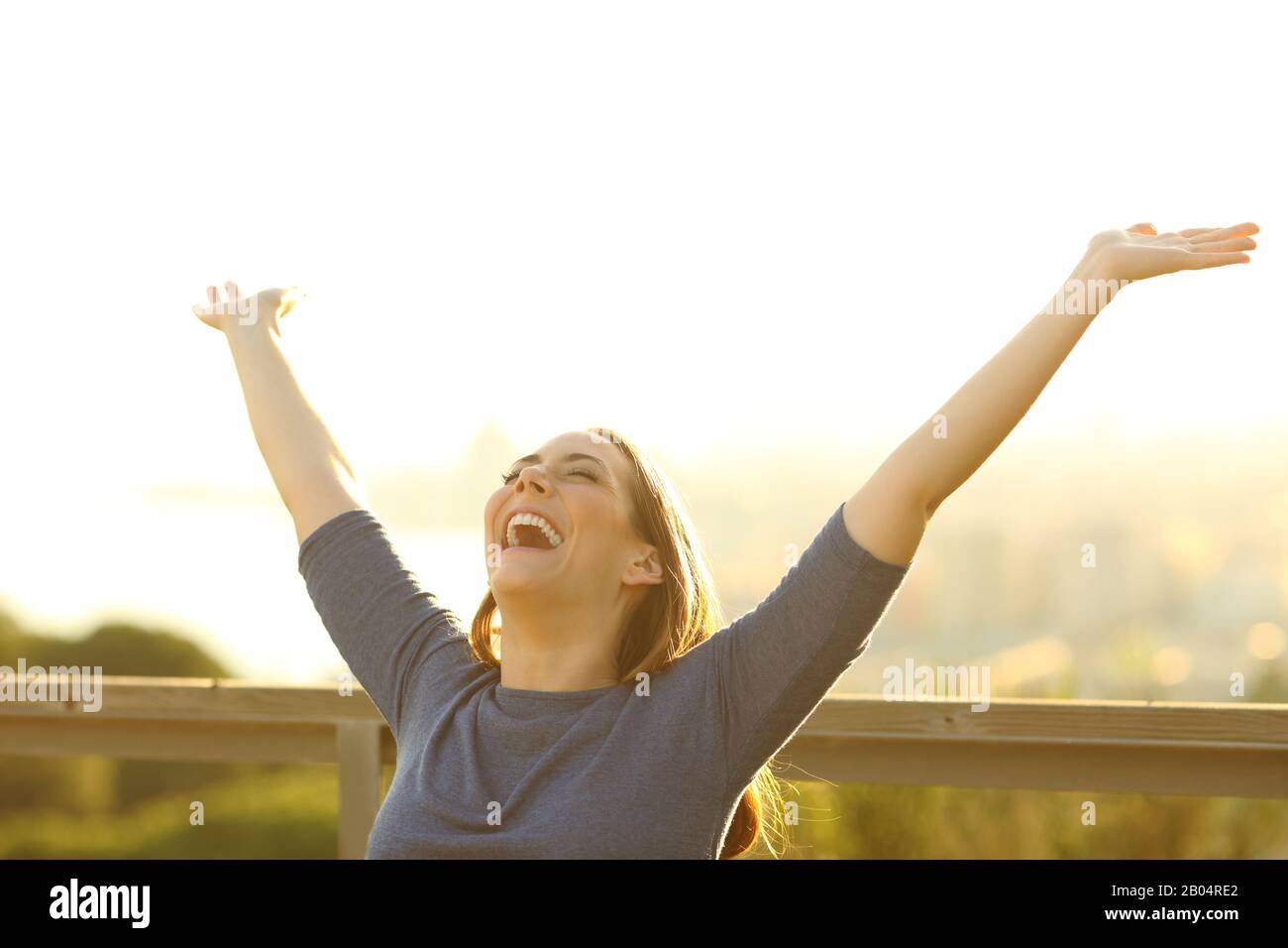 Happy woman sitting on a bench raising arms celebrating life in a park ...