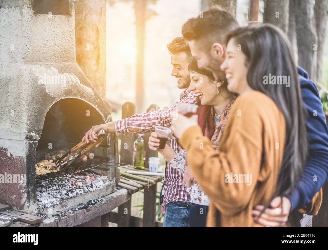 Happy friends cooking meat and drinking wine at barbecue outdoor ...