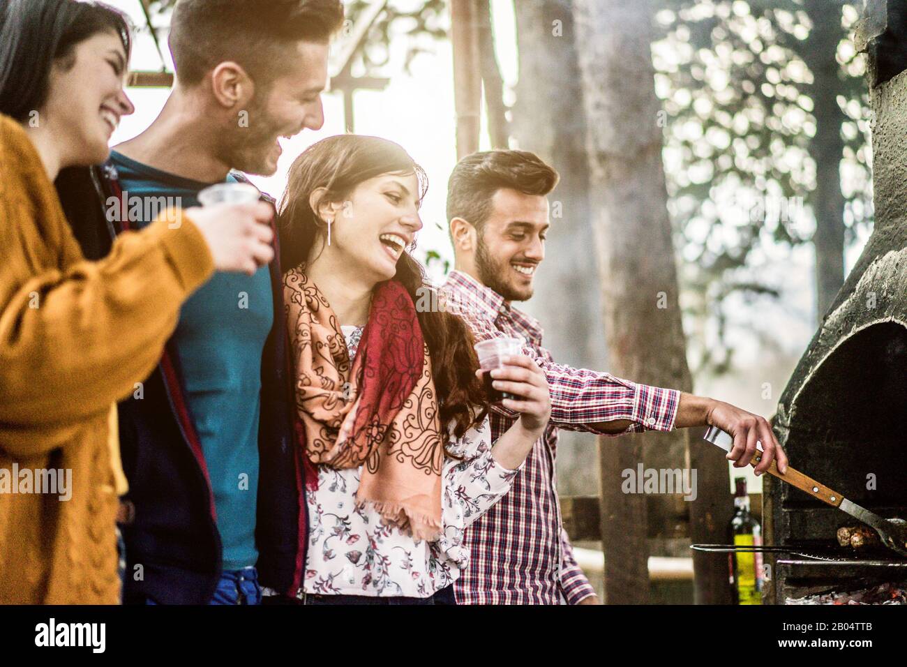 Happy friends eating sausages and drinking wine at barbecue outdoor ...