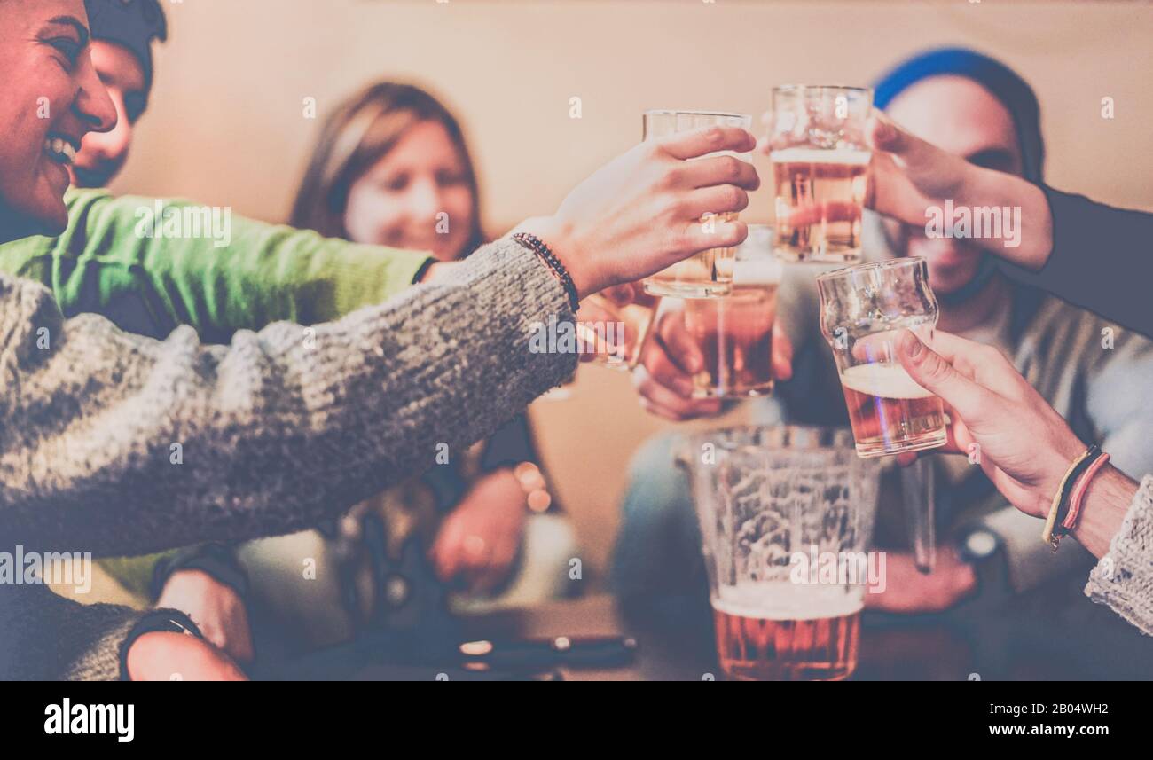 Happy friends toasting beers and laughing at chalet pub in mountains ...