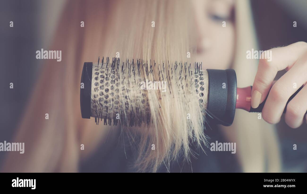 Round brushing combs long blond hair. Background face of a girl in blur ...