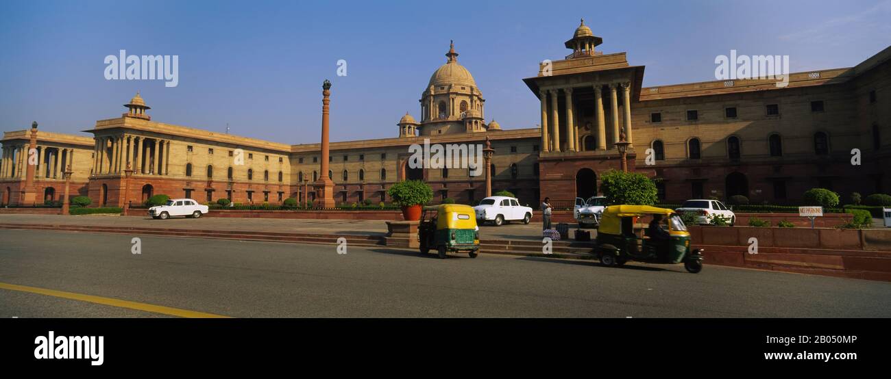 Cars and autorickshaws on the road with a government building in the ...