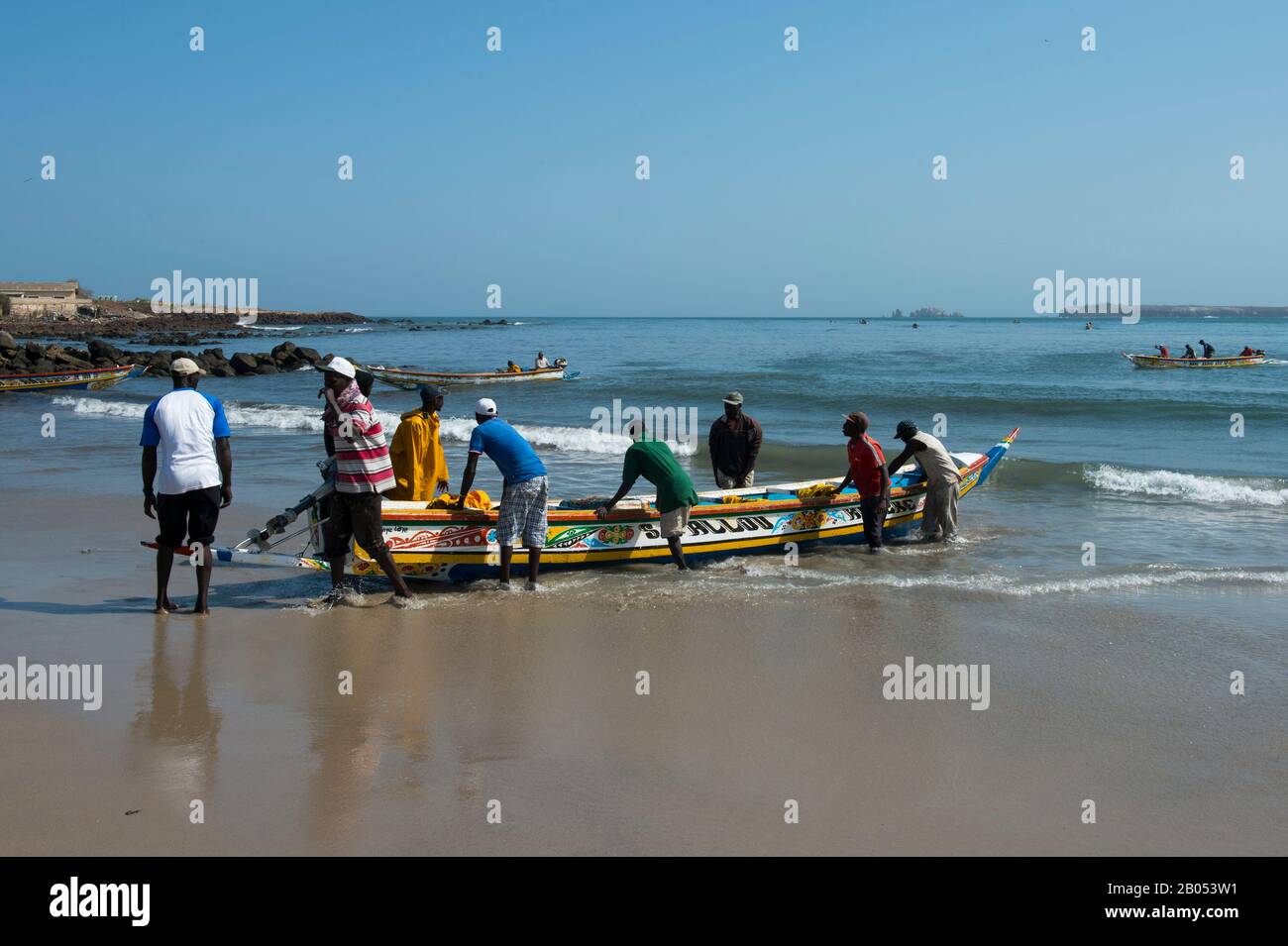 Fishermen pulling colorful fishing boat onto beach at Soumbedioune, one ...