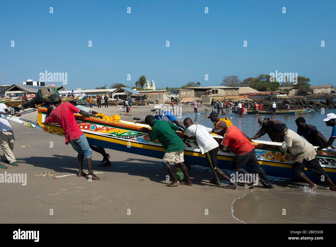 Fishermen pulling colorful fishing boat onto beach at Soumbedioune, one ...