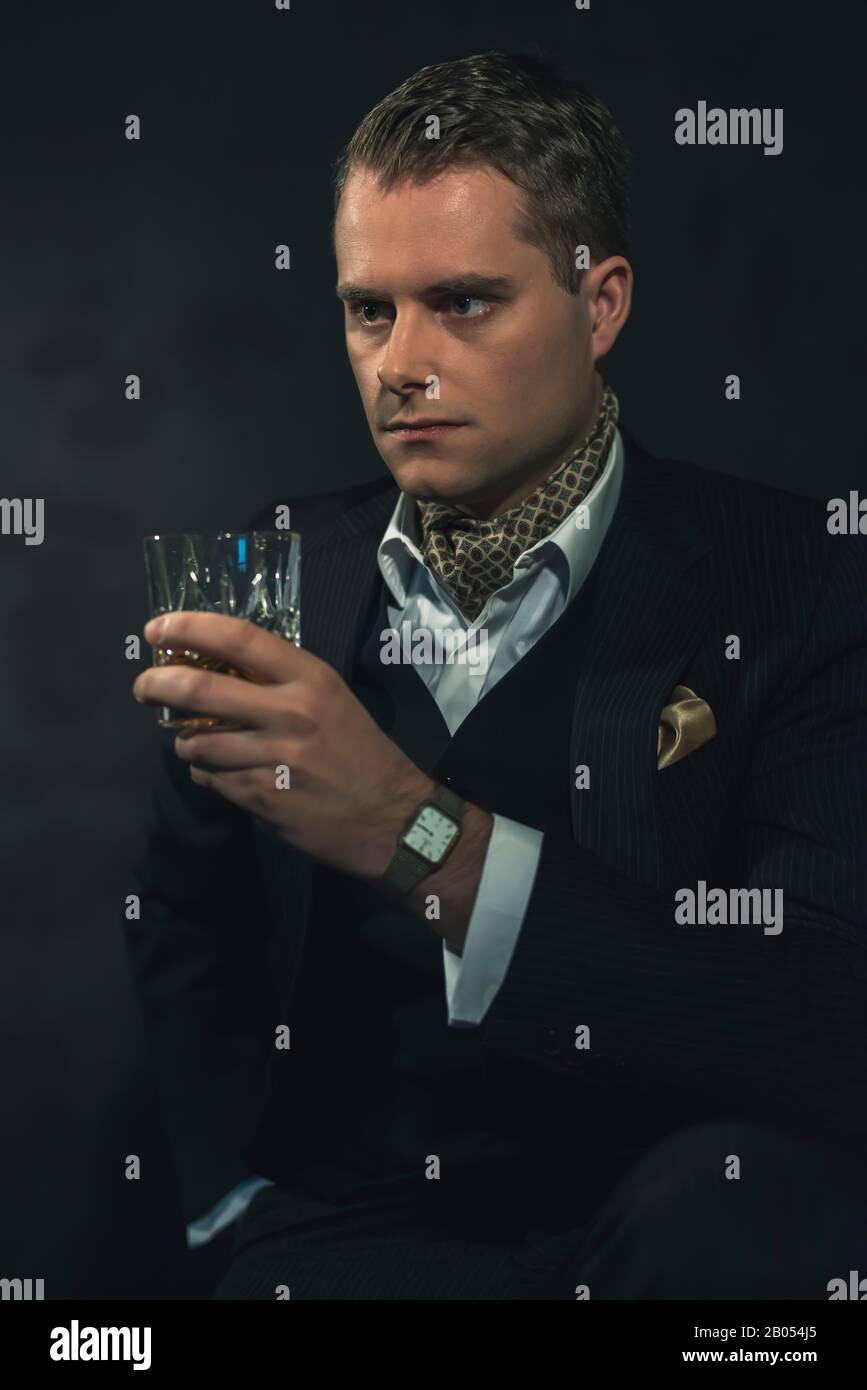 Retro fashion man in dark suit holds a glass of whiskey Stock Photo - Alamy