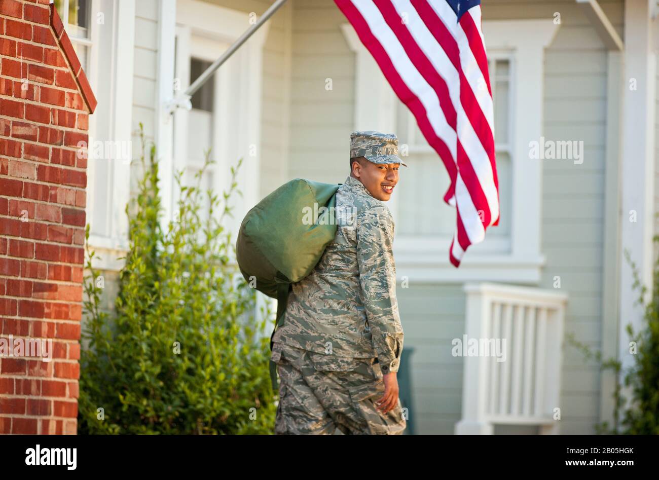 Portrait of a smiling young army soldier carrying a duffel bag outside ...