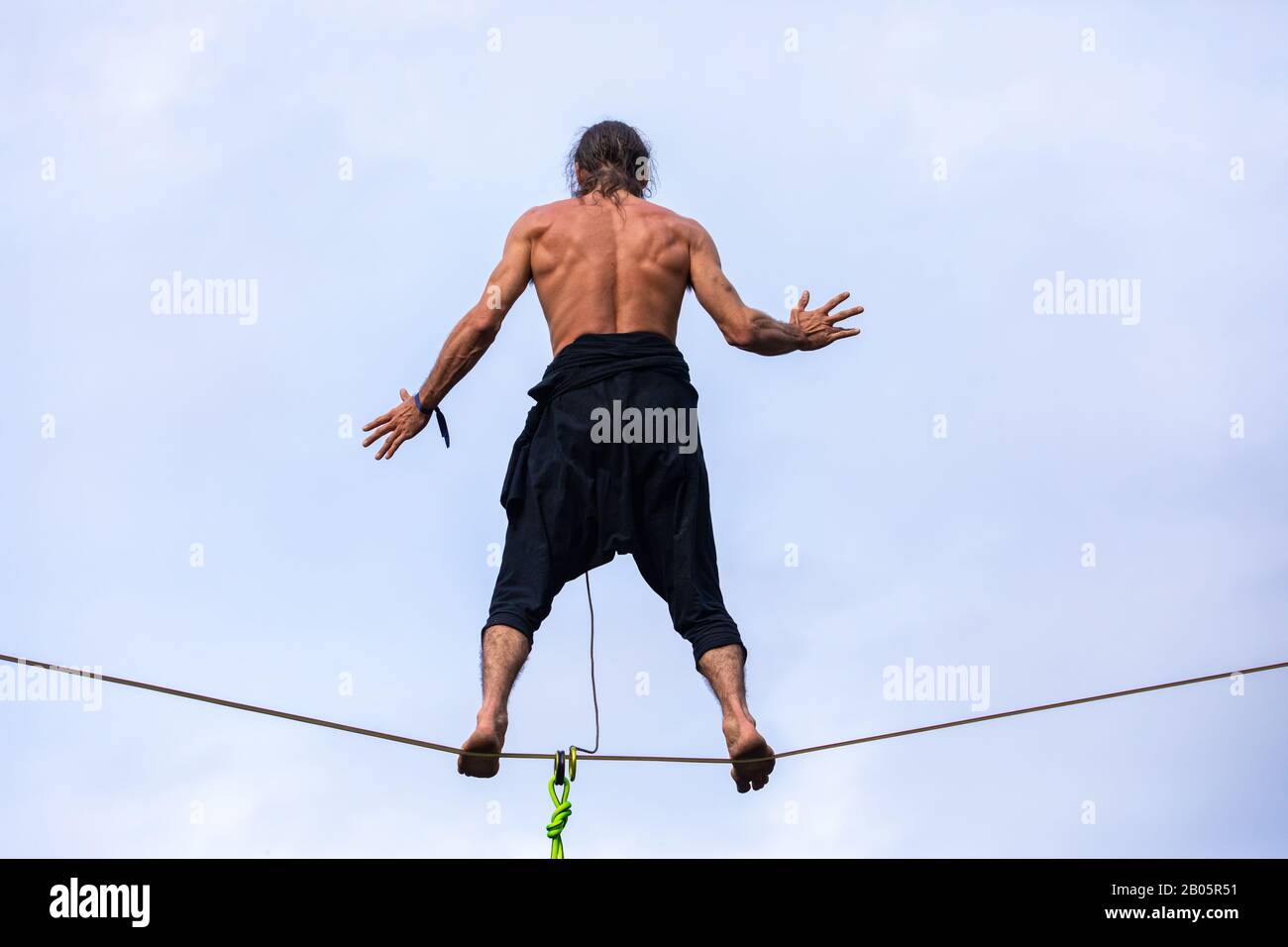 A close up and rear view of a guy standing on a slackwire during a ...