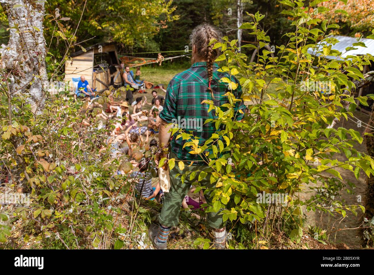 A chubby man is seen from the back, standing amongst trees in a forest ...