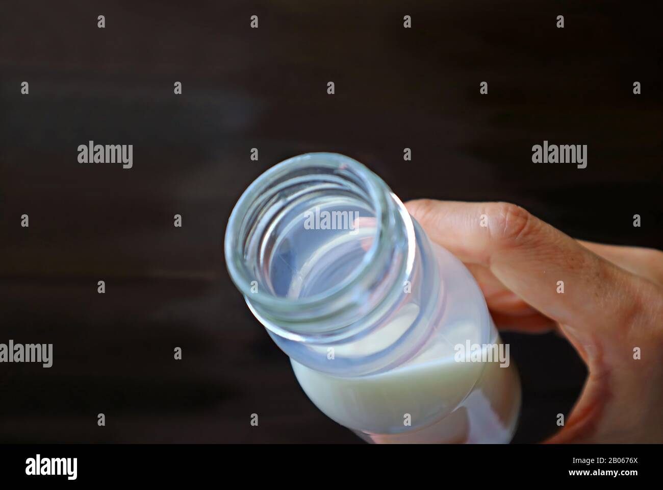 Man's hand holding opened bottle of milk on dark brown background Stock ...