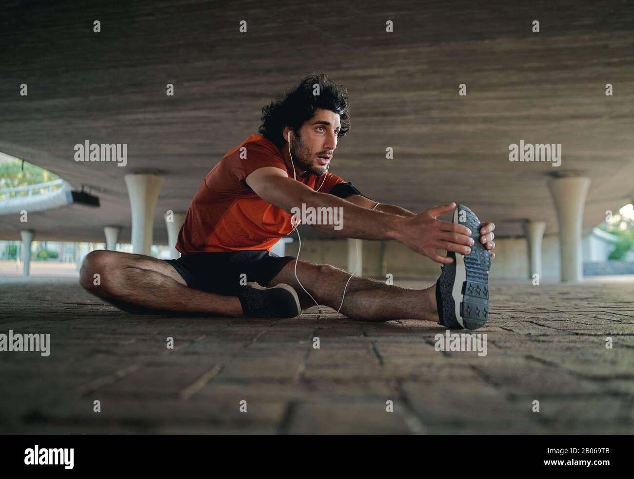 Fit young man in sportswear sitting on pavement under the bridge ...