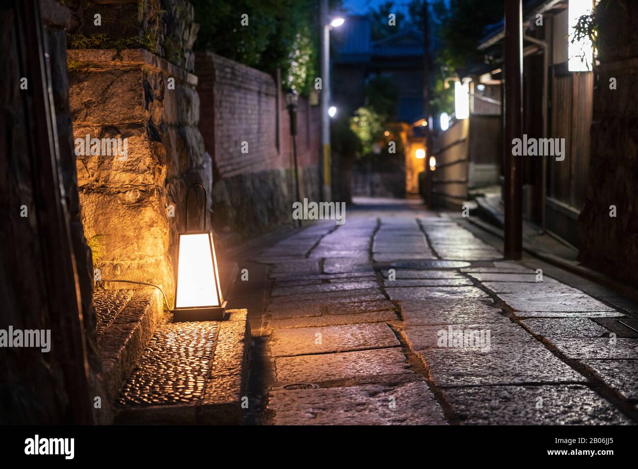 Lamps illuminate old stone road through traditional Japanese ...