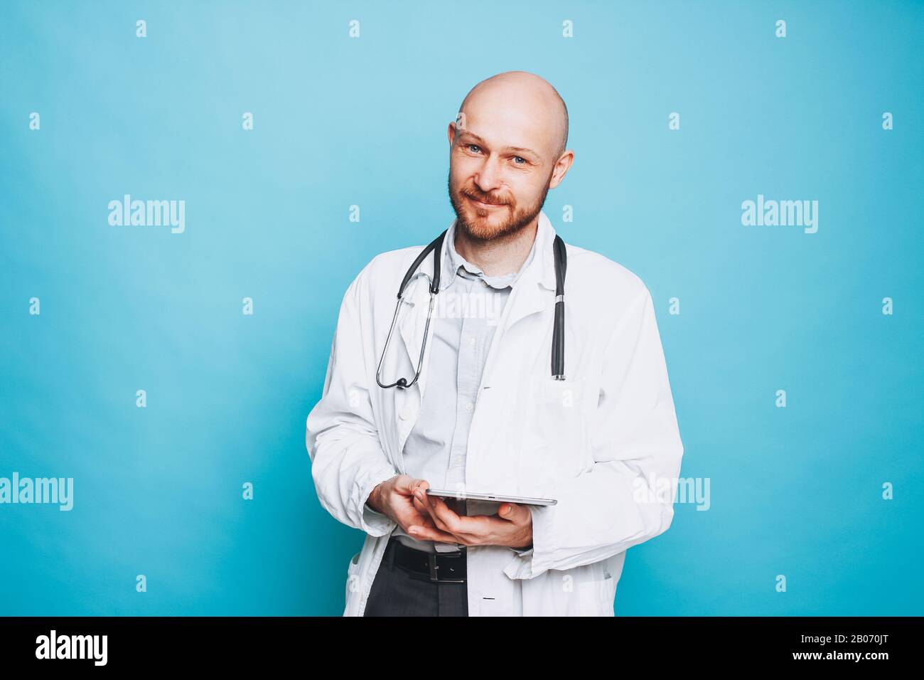 Attractive friendly bald bearded smiling doctor with tablet looking at ...