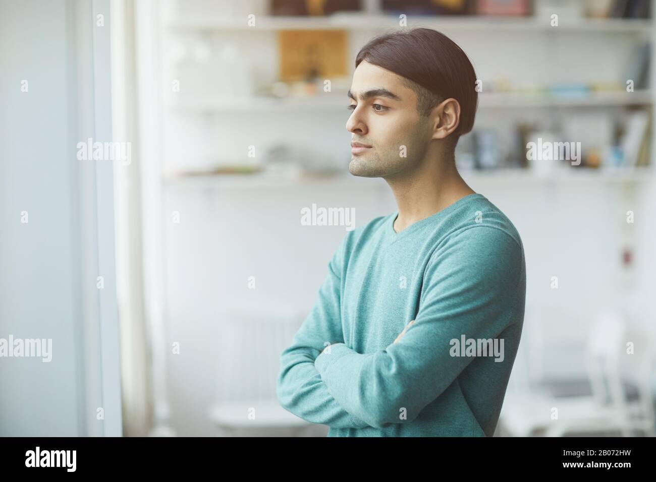 Young pensive man standing with arms crossed looking away and thinking ...
